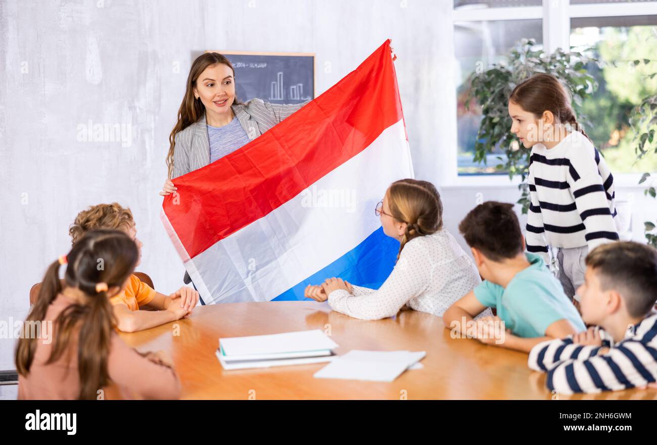 Teacher holds the flag of Netherlands in her hands and tells students ...