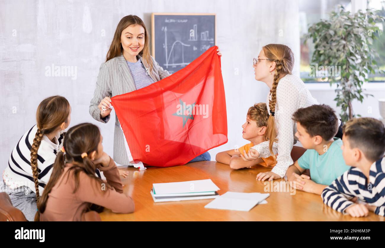 Group of curious preteen learners and young female teacher with flag of ...