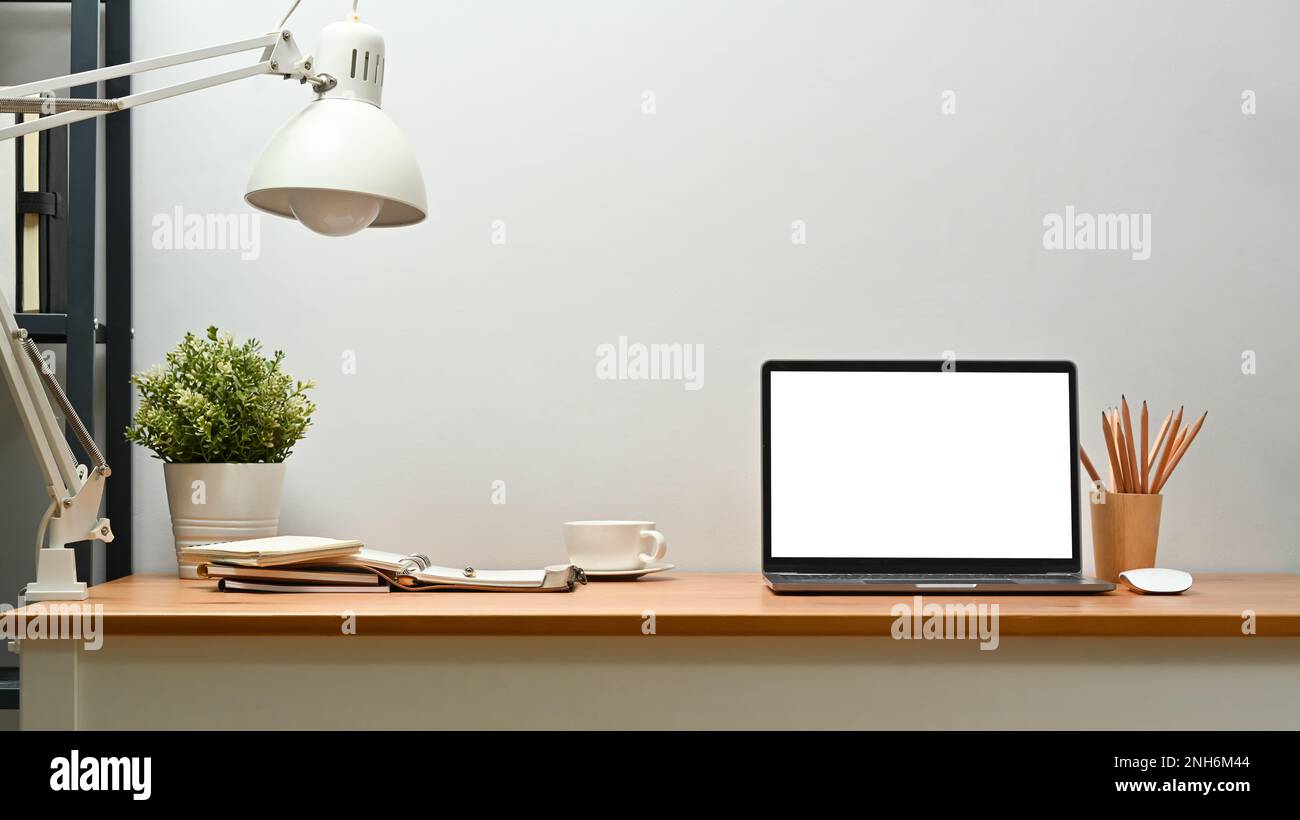 Front view of laptop, potted plant, lamp and supplies on wooden desk ...