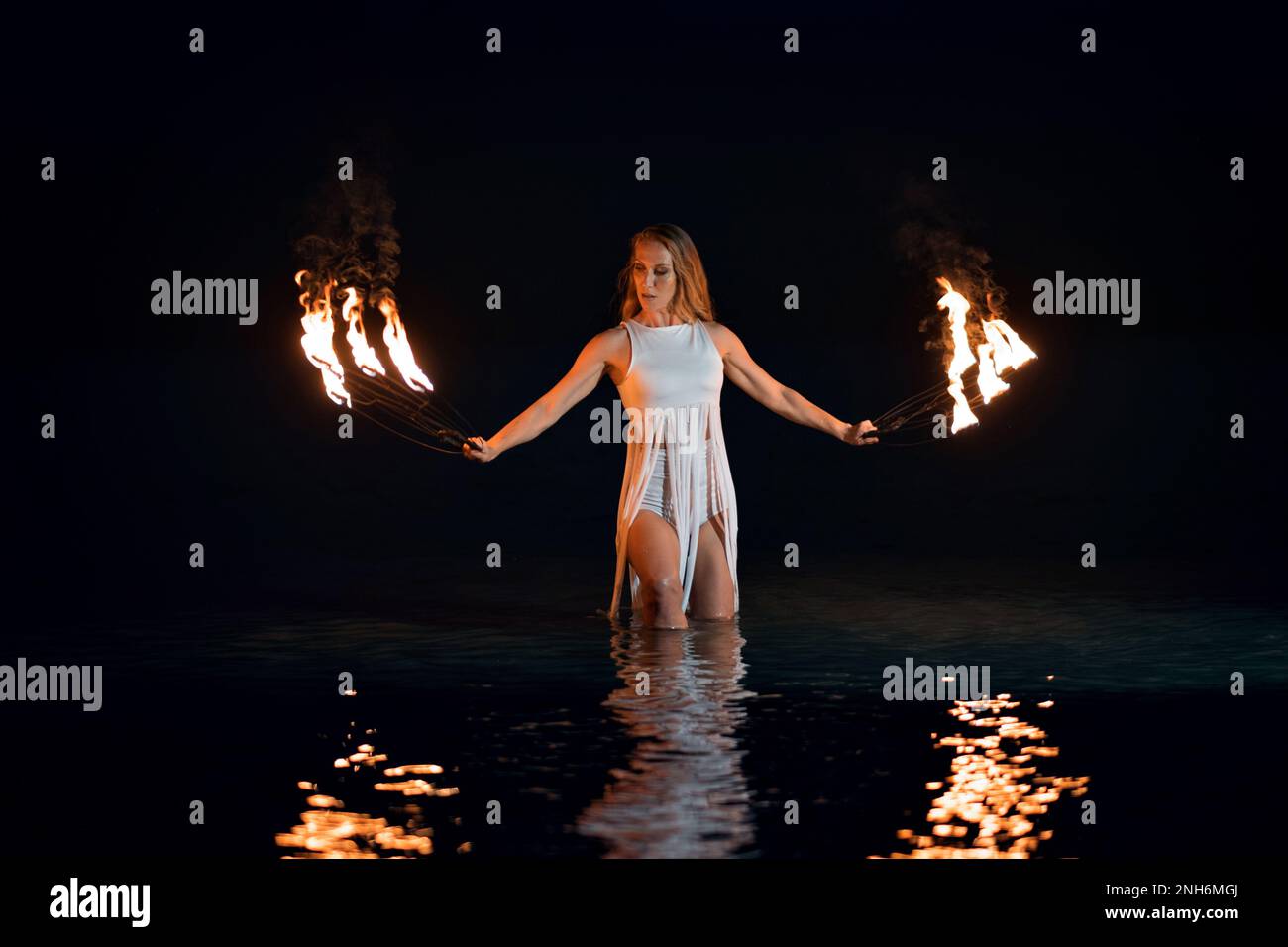 Caucasian woman dancing with fire in the water. Fire show at sea ...