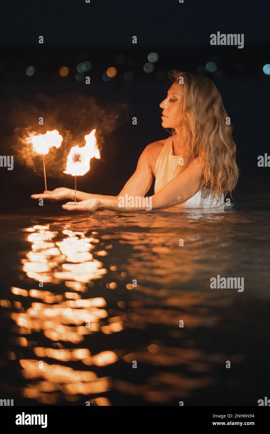 Caucasian woman dancing with fire in the water. Fire show at sea ...
