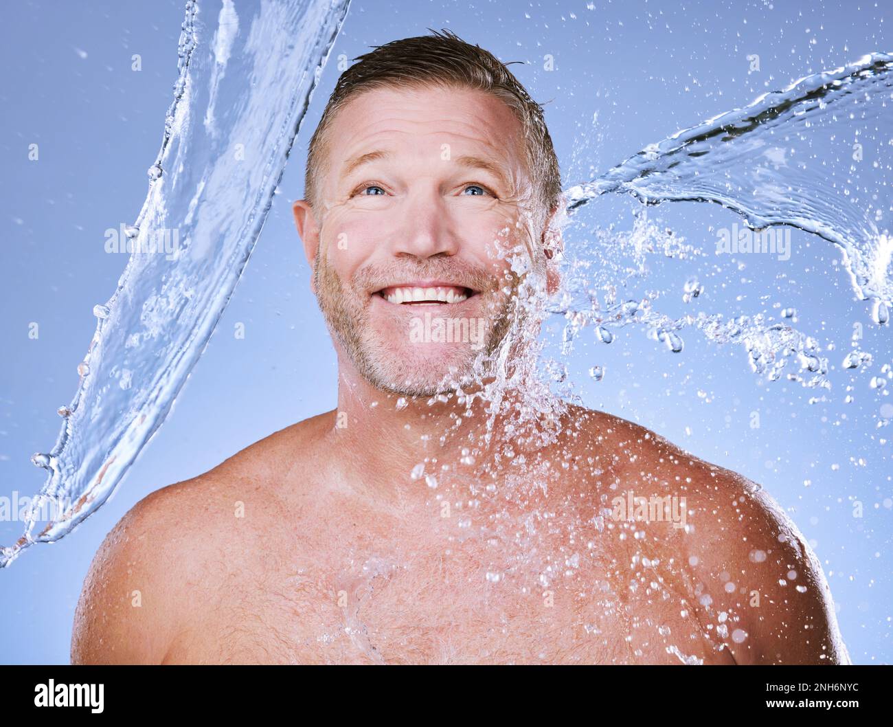 Showering, water splash and man with smile, cleaning and daily hygiene on blue studio background ...