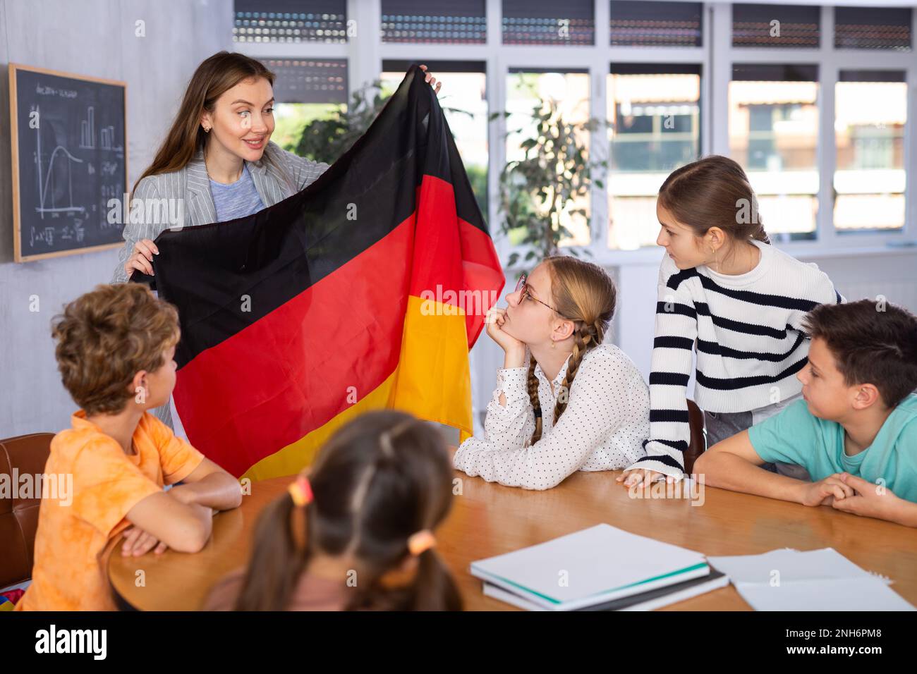 Group of curious preteen learners and smiling young female teacher with ...