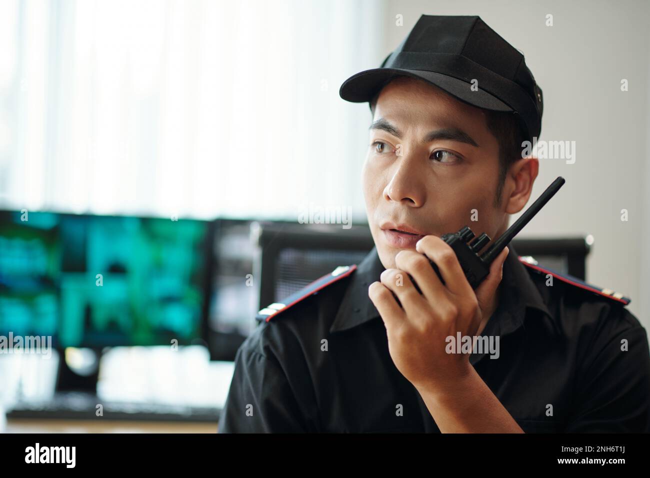 Portrait of security guard speaking in walkie-talkie and looking away ...