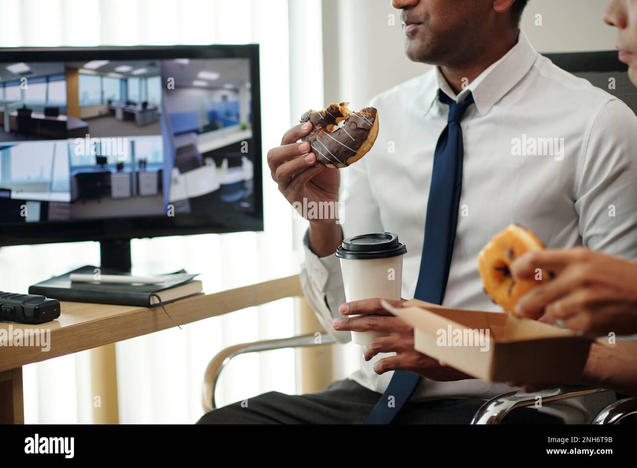 Cropped image of security guards eating sweet donuts when watching ...