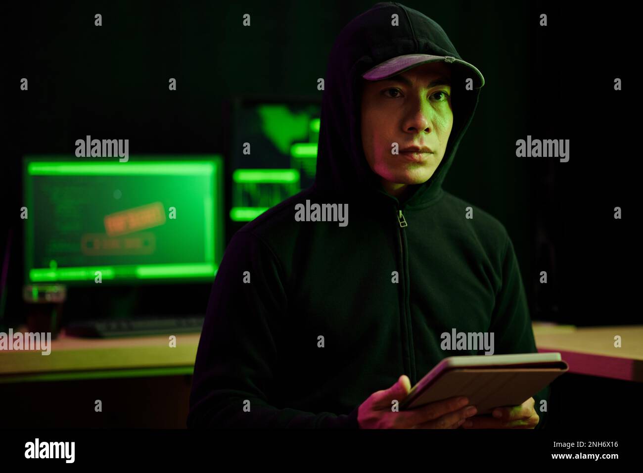 Serious hacker in cap and black hoodie holding tablet computer Stock ...