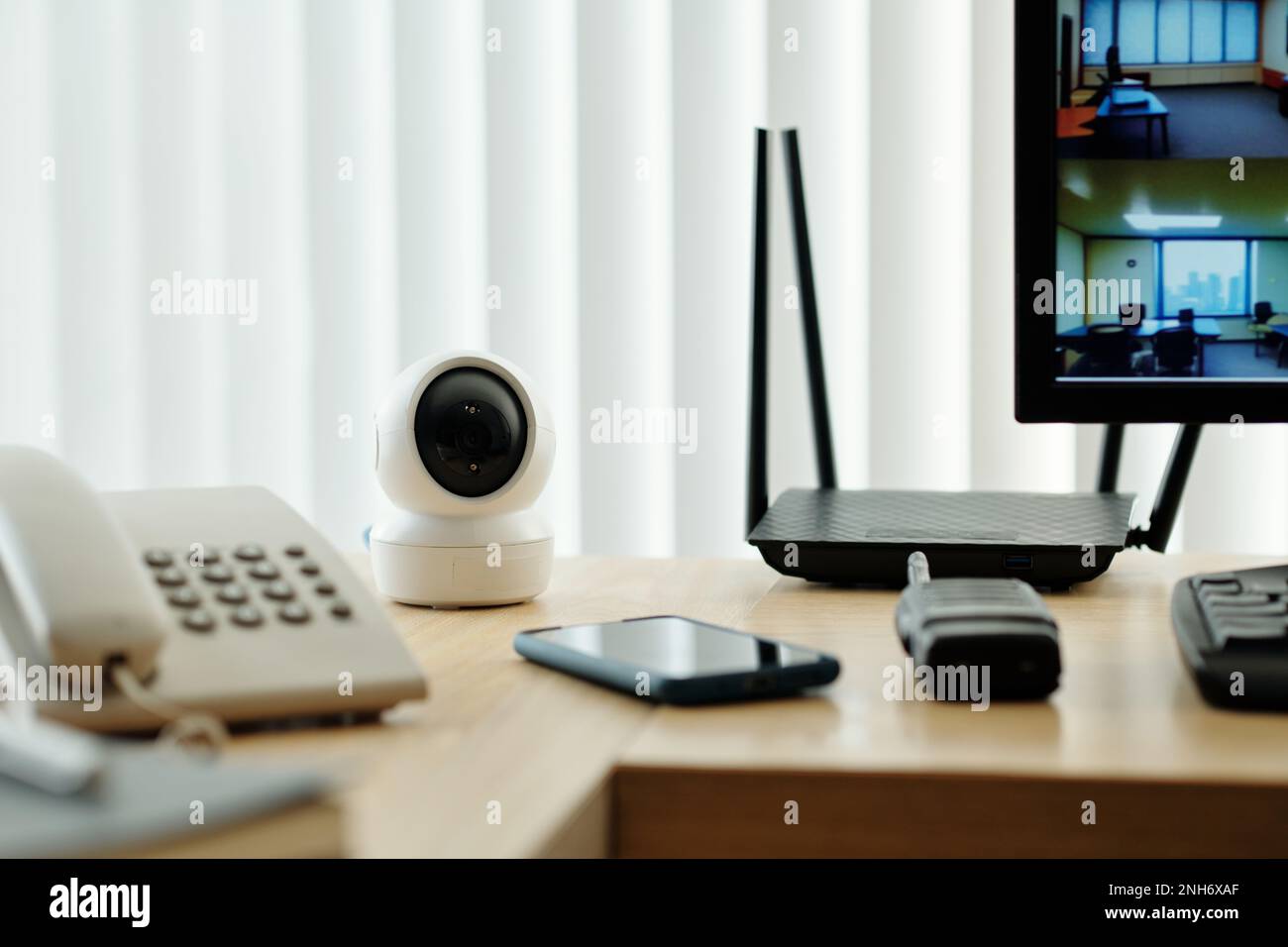 Surveillance camera, router and telephone next to monitor on desk of ...