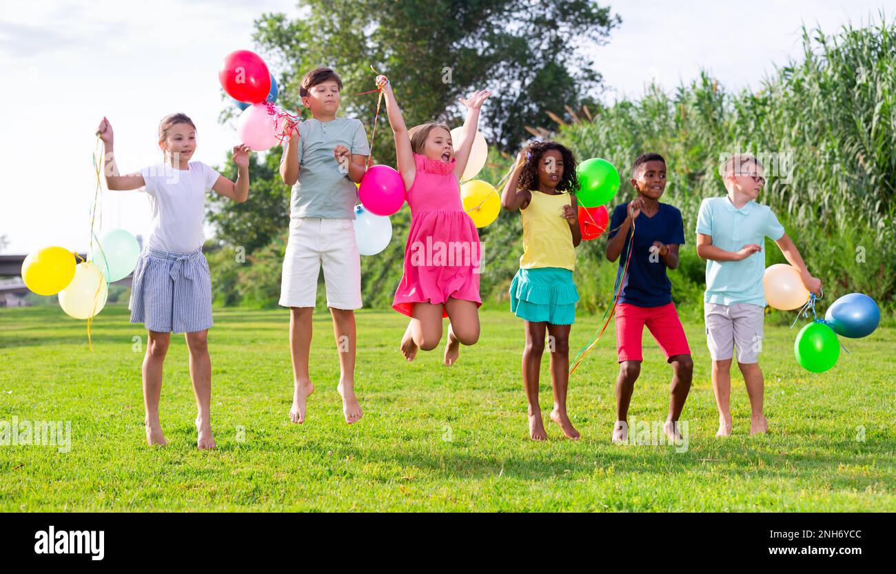 Kids with balloons jumping on field Stock Photo - Alamy