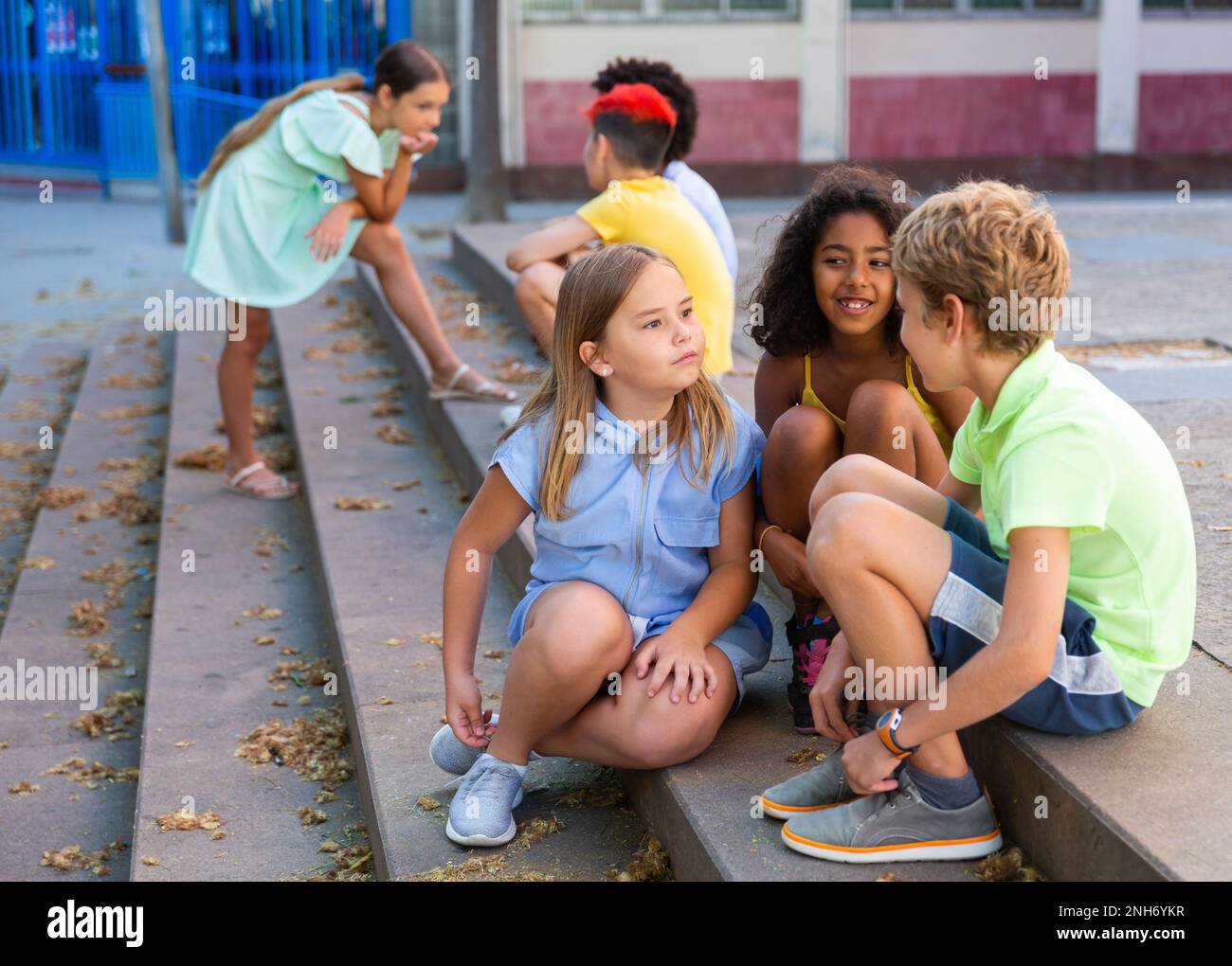 Cheerful preteen girls and boys sitting on steps outdoors and chatting ...