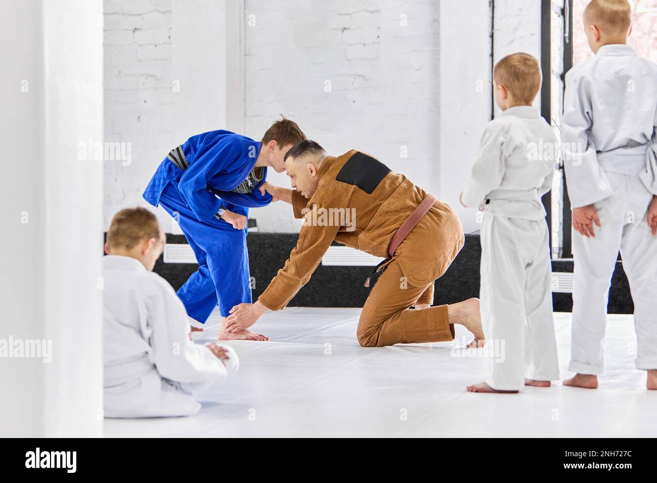 Teacher showing mix fight tricks to children, learning judo, jiu-jitsu fight activity. Sportive ...
