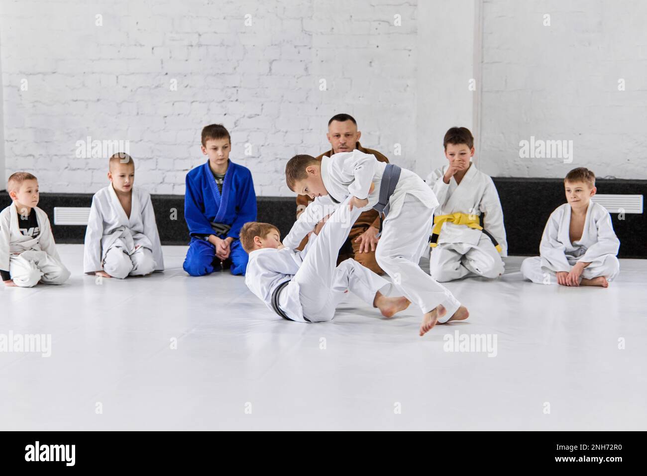 Boys, children in white kimono training judo, jiu-jitsu indoors with professional coach ...