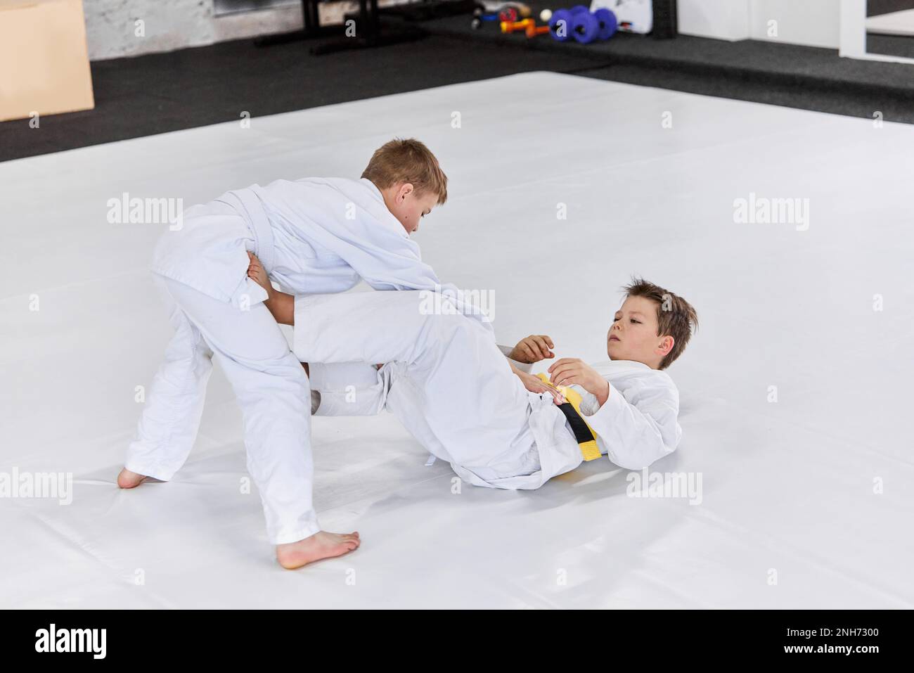 Two boys, children in white kimono training judo, jiu-jitsu fight style indoors. Developing ...