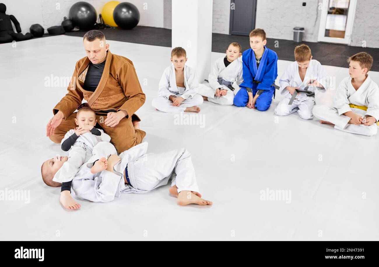 Boys, children in white kimono training judo, jiu-jitsu fight style indoors with coach ...
