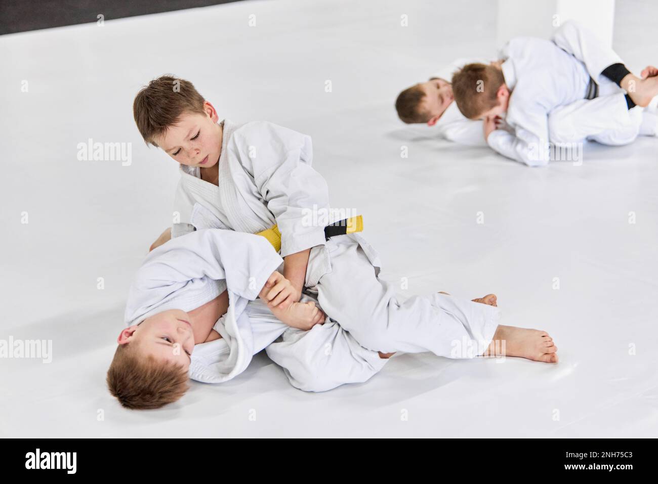 Boys, children in white kimono training, practising judo, jiu-jitsu exercises indoors ...