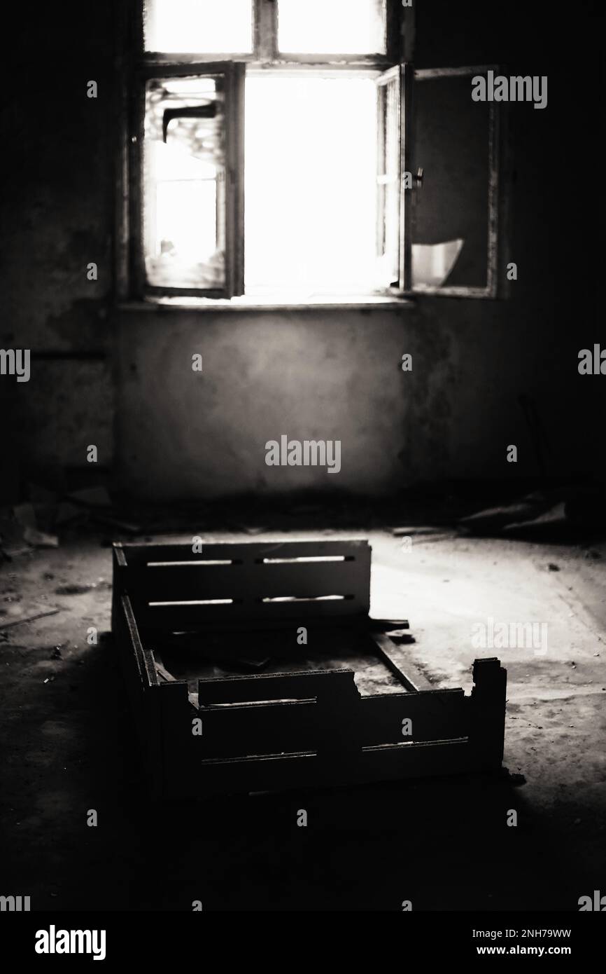 Small broken bed in a ruined room with backlight, black and white shot ...