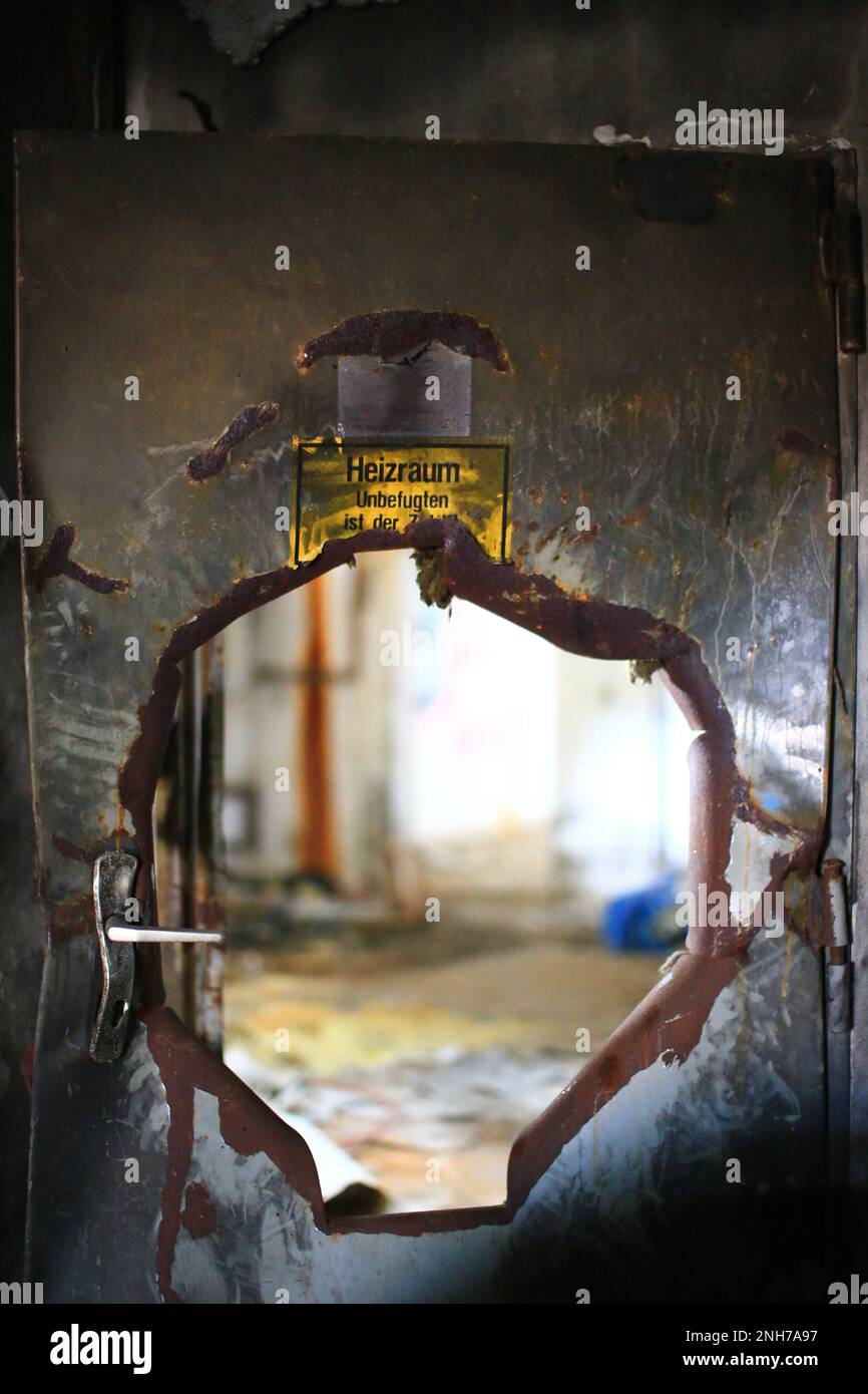 Burst, bent door with sign: Heizraum - Unbefugten ist der Zutritt ...