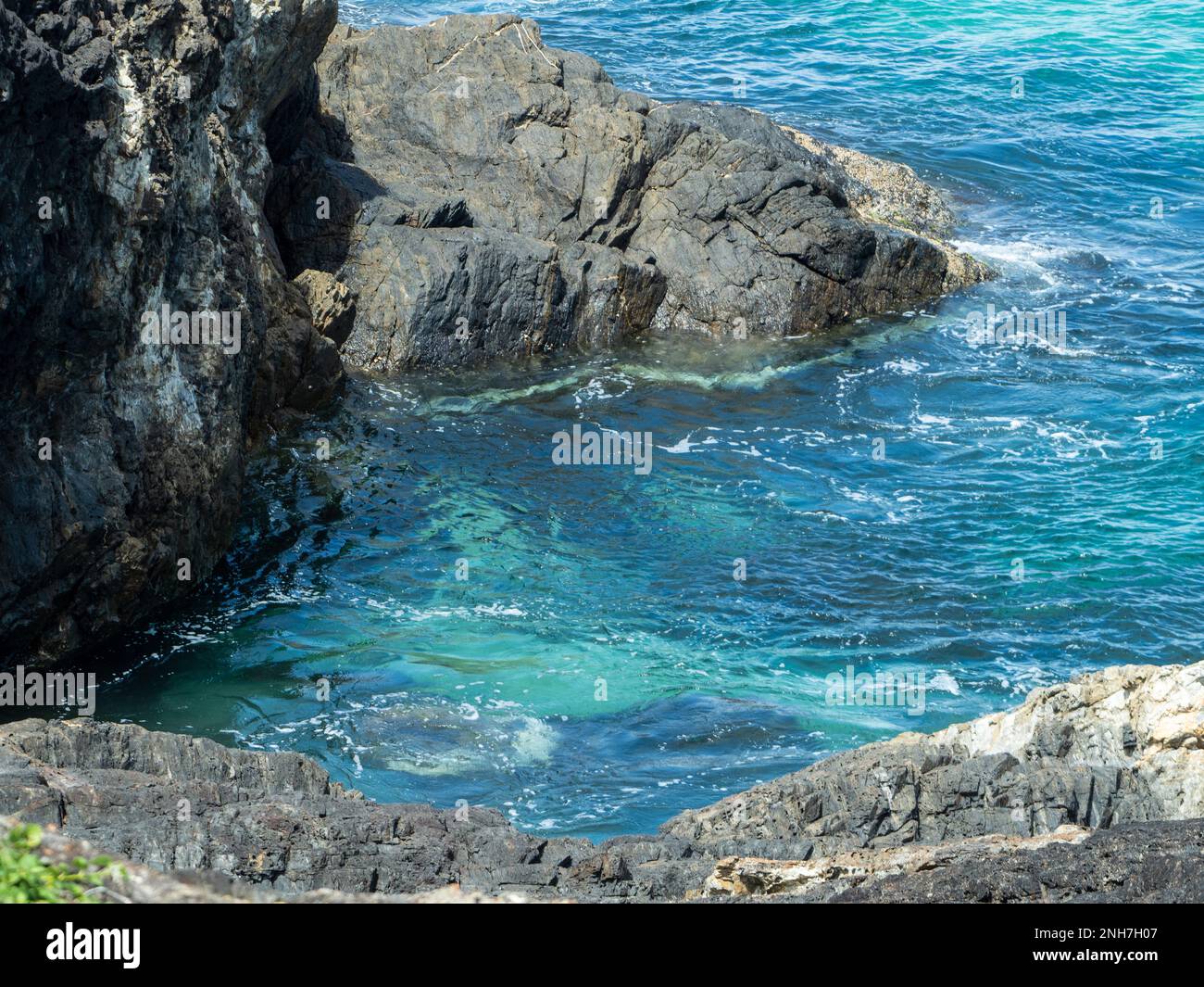 Clear glassy azure blue sea water swirling gently around rocks at the ...