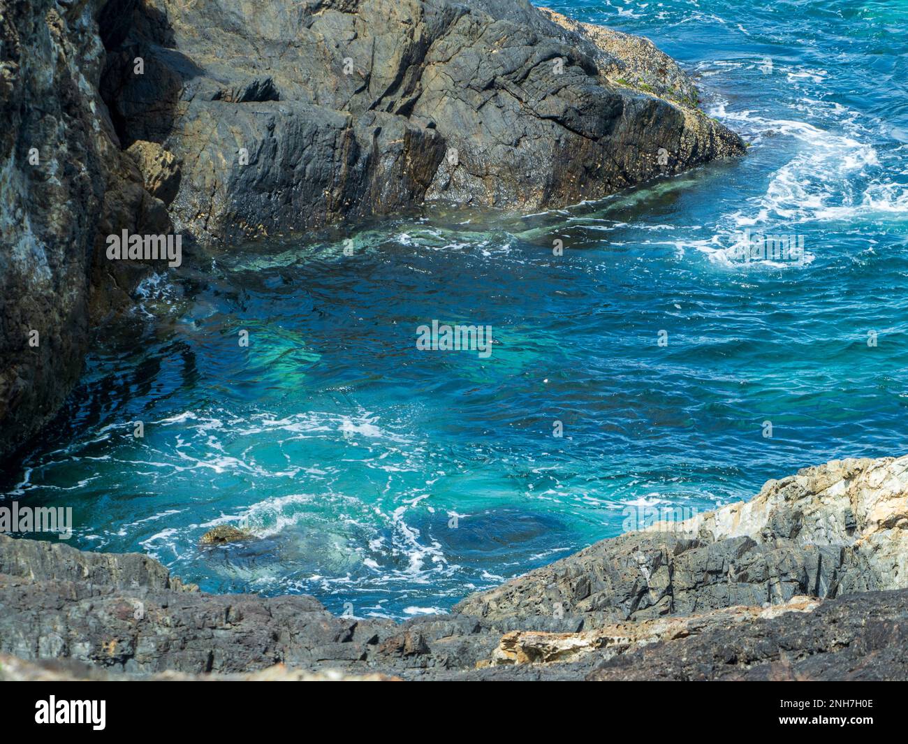 Clear glassy azure blue sea water swirling gently around rocks at the ...