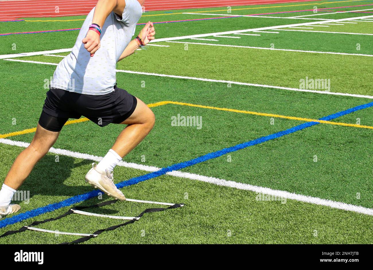 High school football player running though the ladder during summer ...