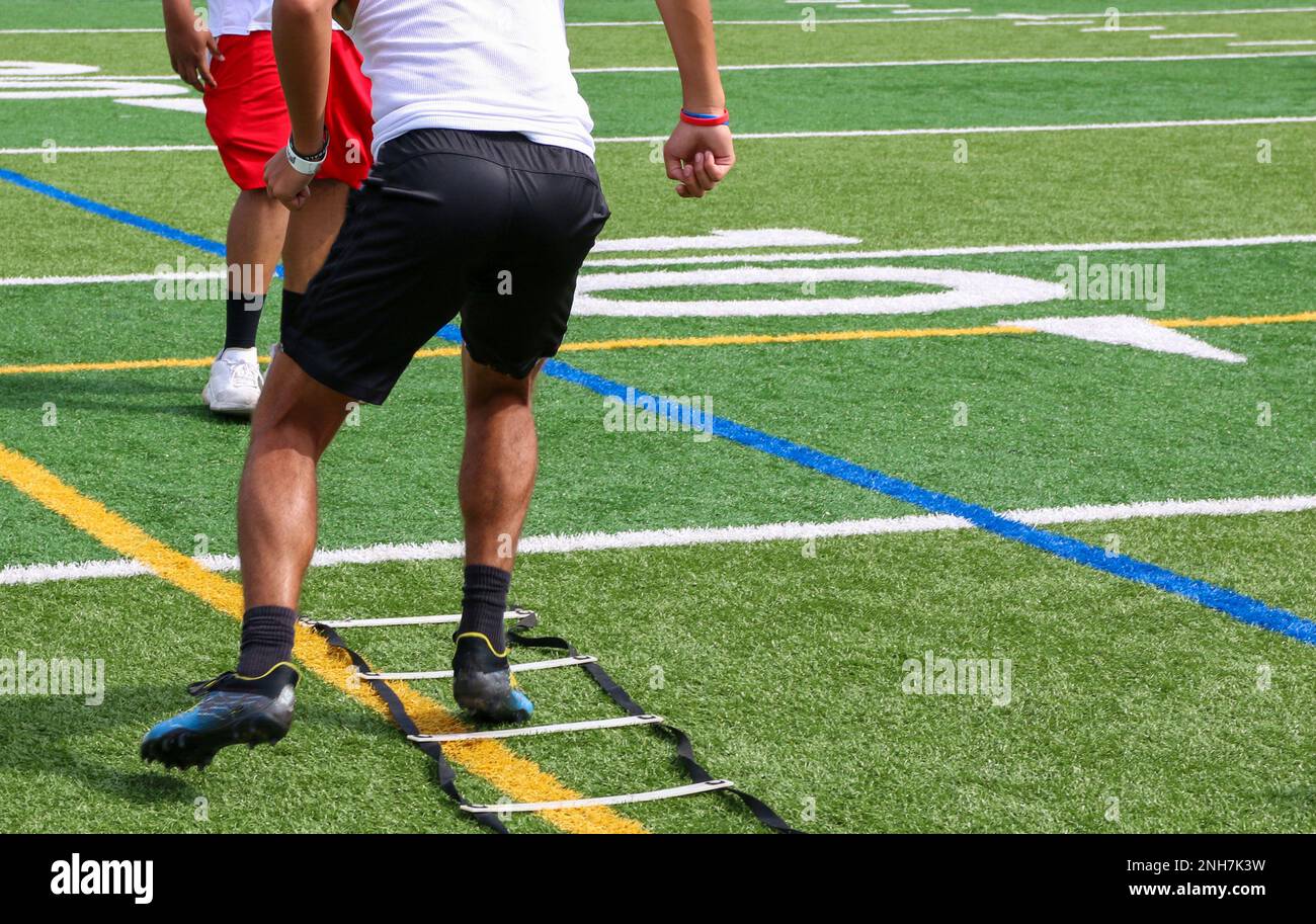 Rear view of a high school football player is running in the ladder ...