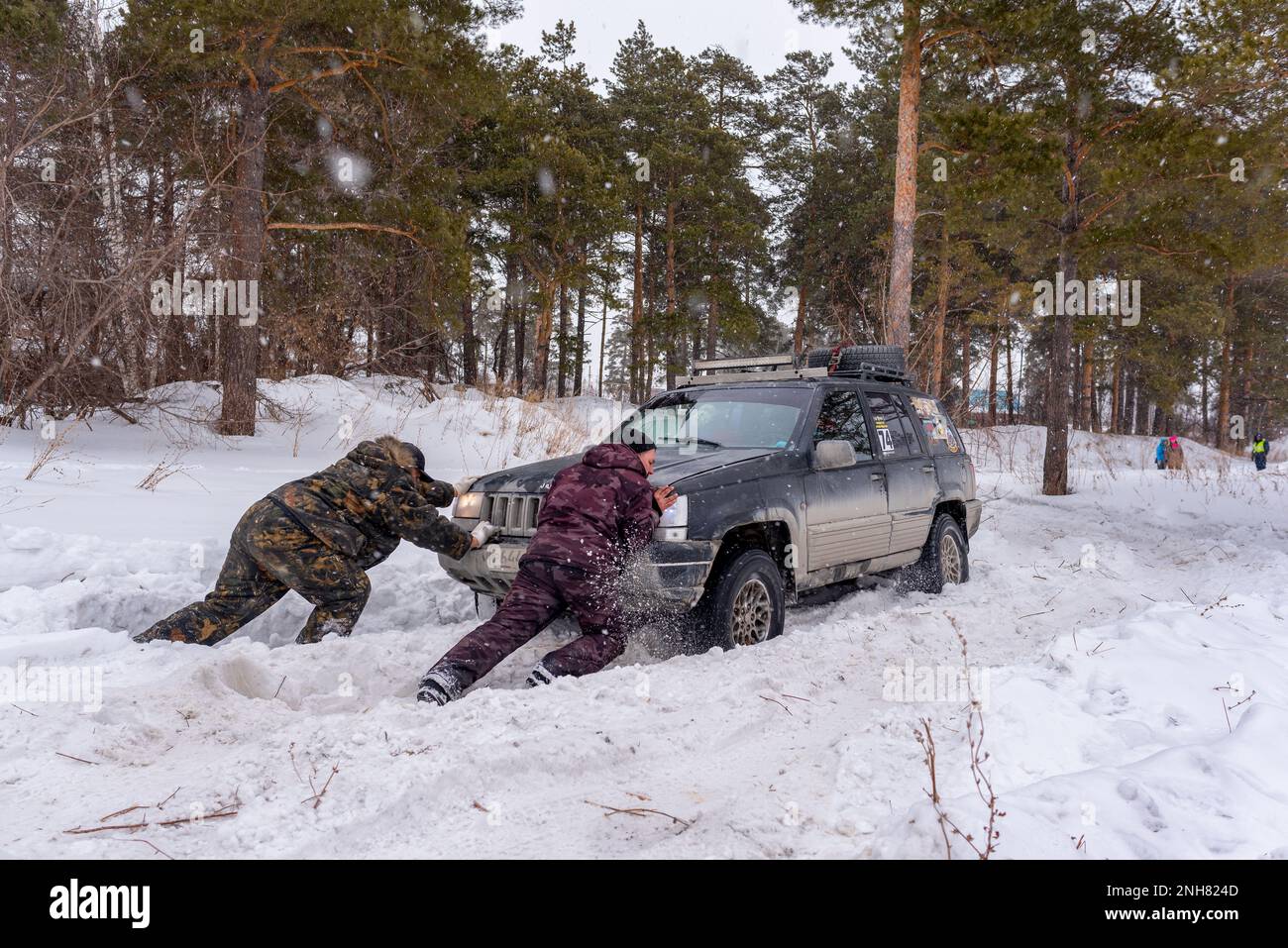 Two unknown men push an off-road SUV "Jeep Grand Cherokee 4x4" stuck in ...