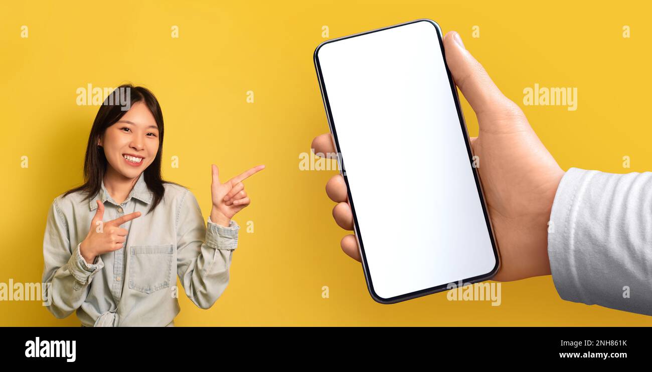 Cheerful young asian lady pointing at huge smartphone in giant male ...