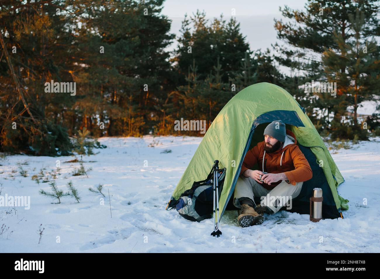 A tourist rests after a hike, sitting near a tent with a cup of coffee ...