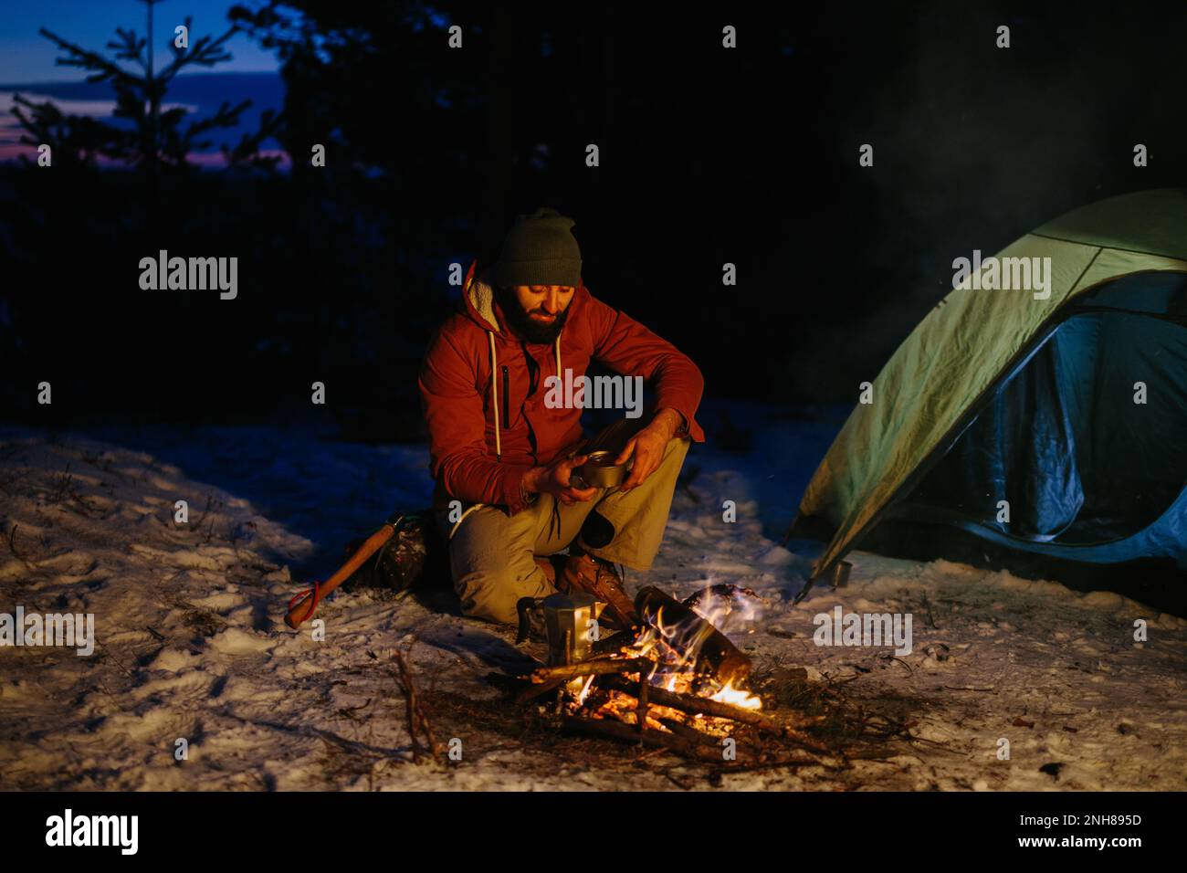 Image of hiker young man cooking dinner by a campfire in the mountains ...