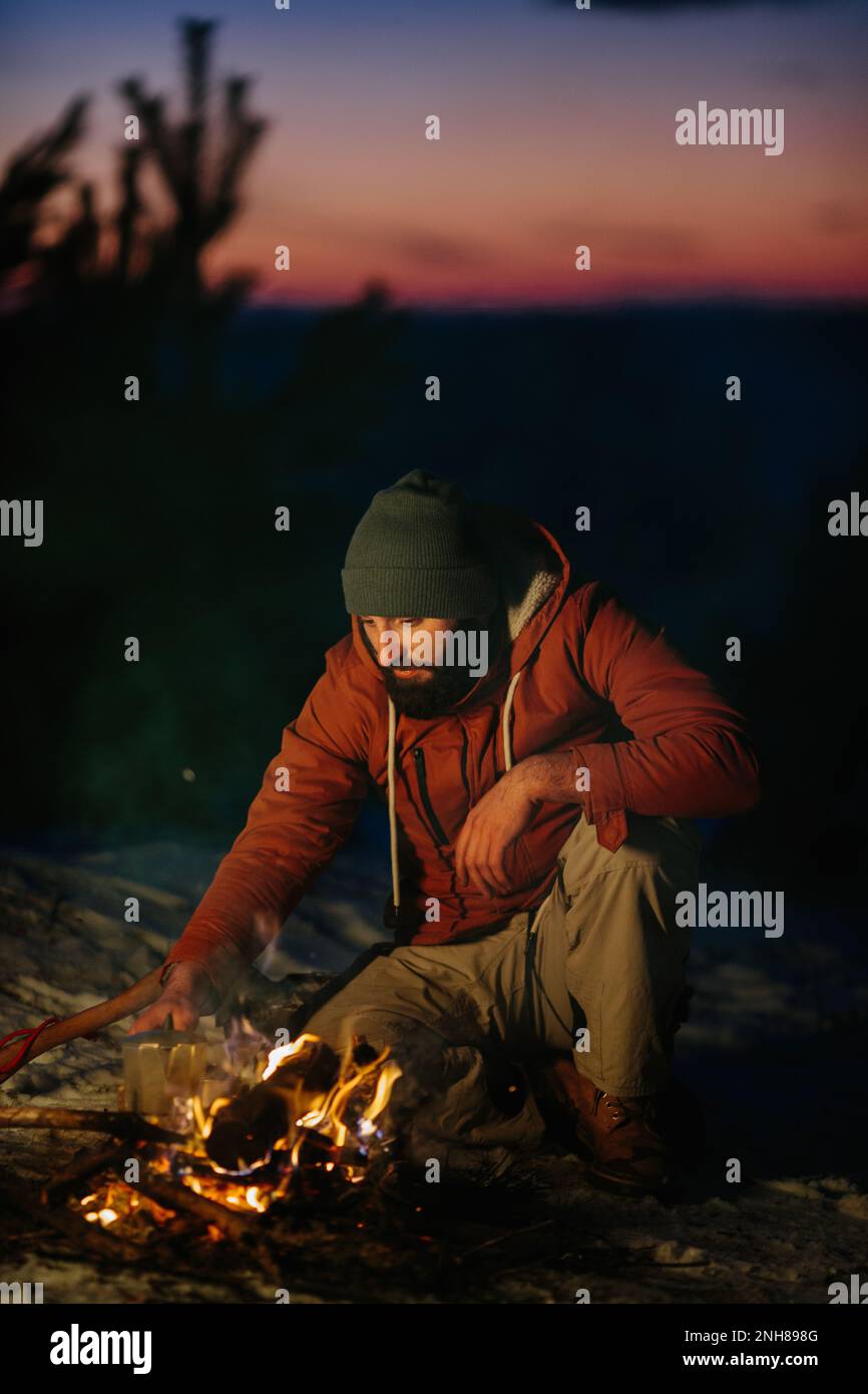 Image of hiker young man cooking dinner by a campfire in the mountains ...