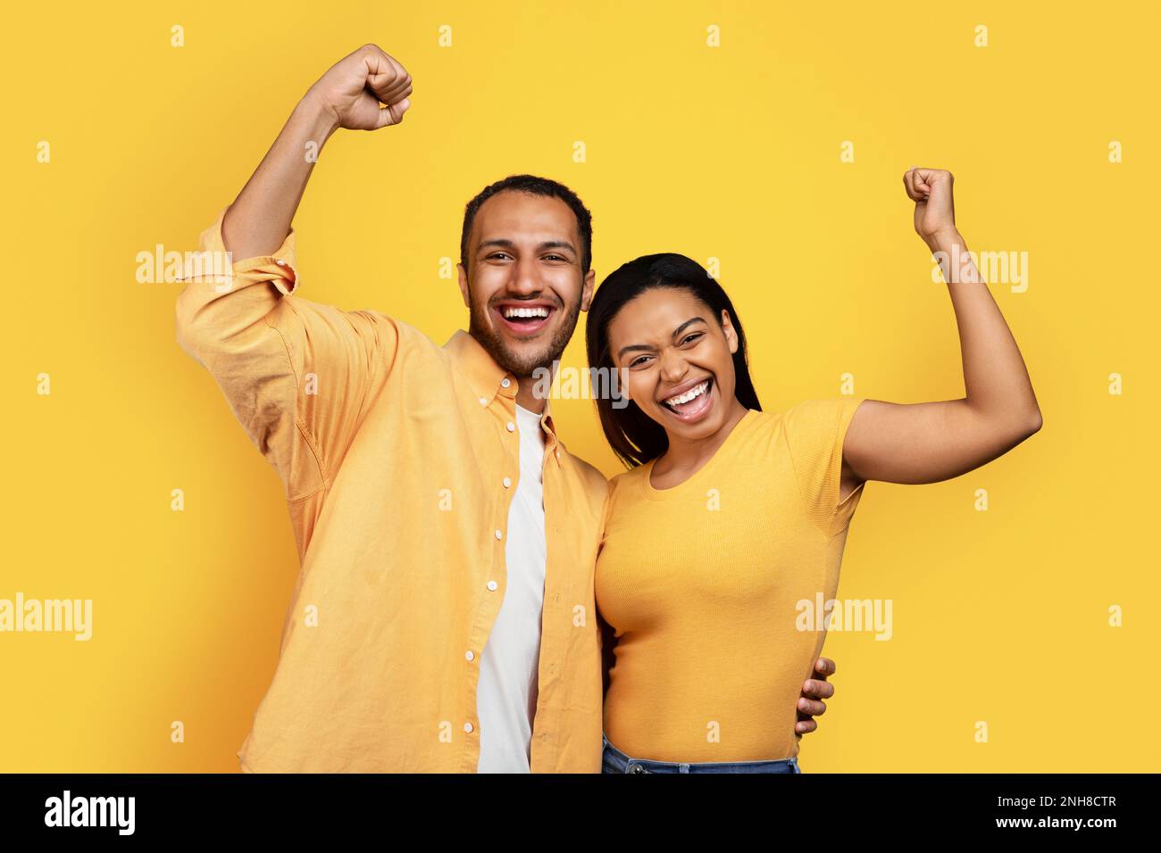 Cheerful young african american guy and woman hug, raise hands and make ...