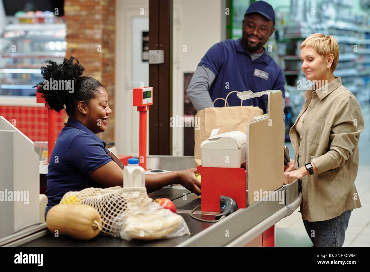 Happy young African American female cashier scanning food products ...