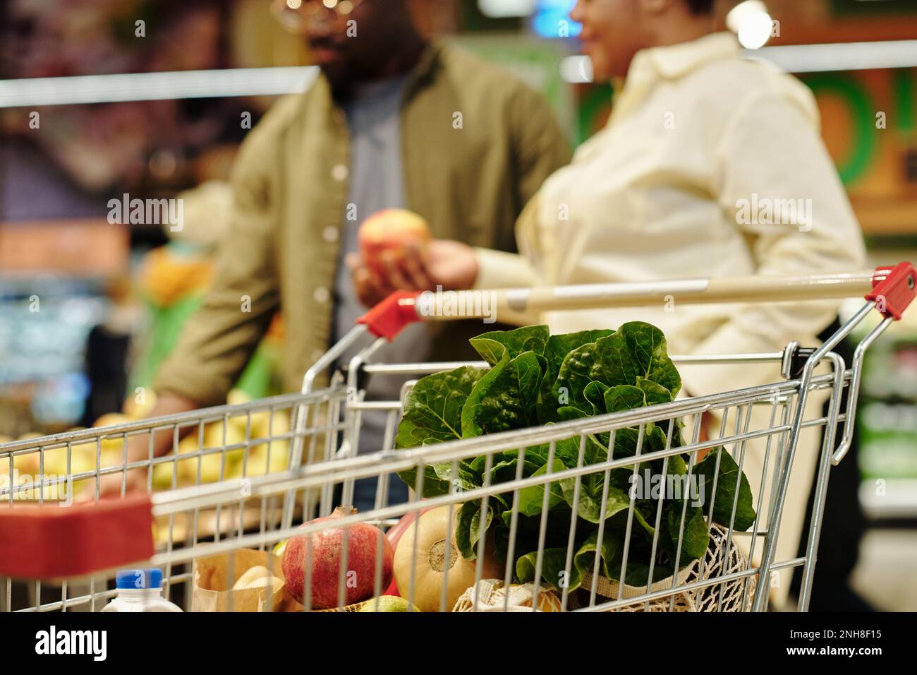 Shopping cart with fresh fruits and vegetables against young couple ...