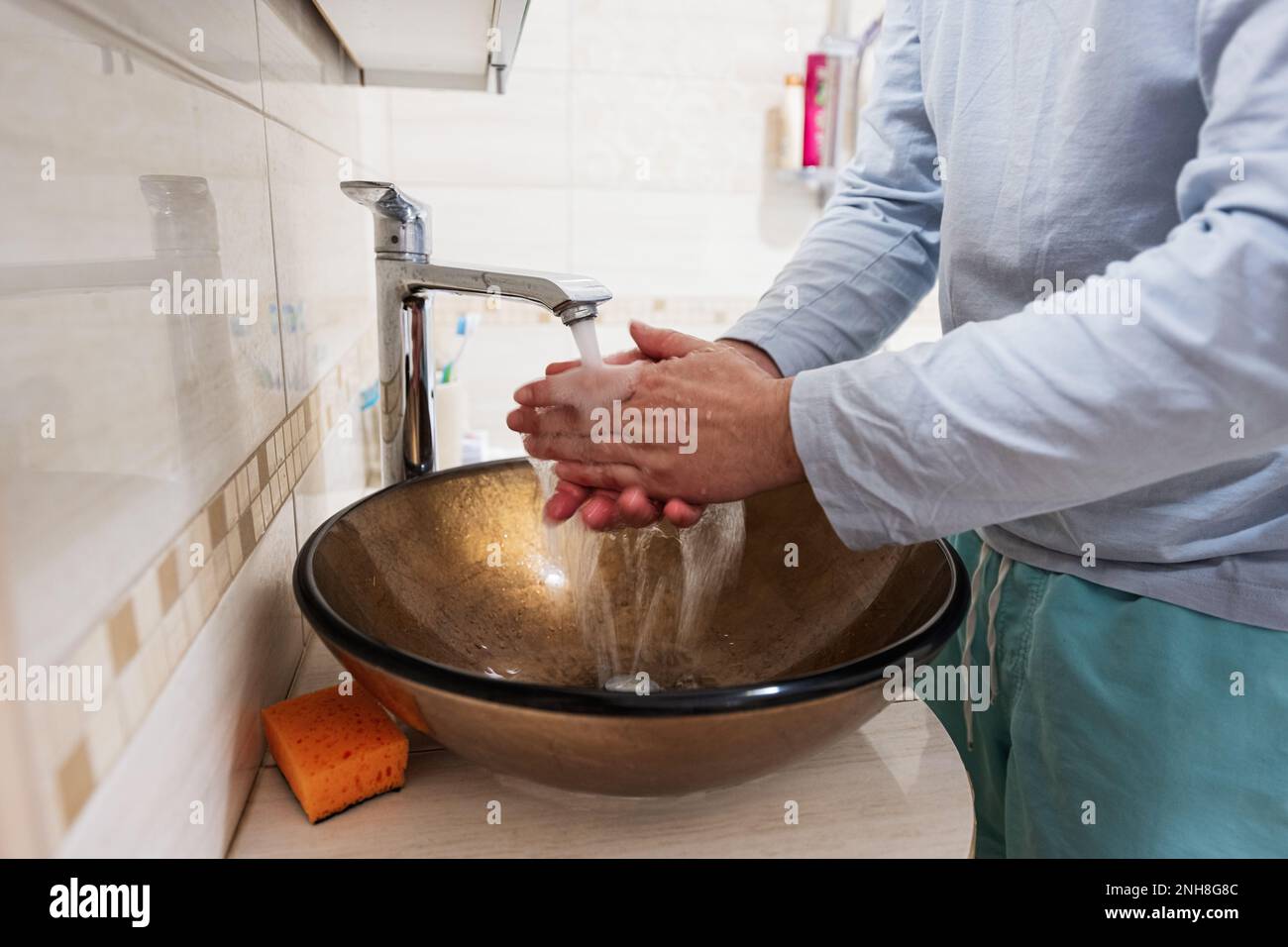 Man washing hands at brown glass hand wash basin with chrome water tap ...
