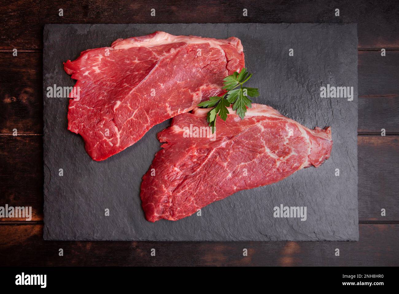 Raw minute steak of marbled beef with a parsley leaf on a stone slate ...