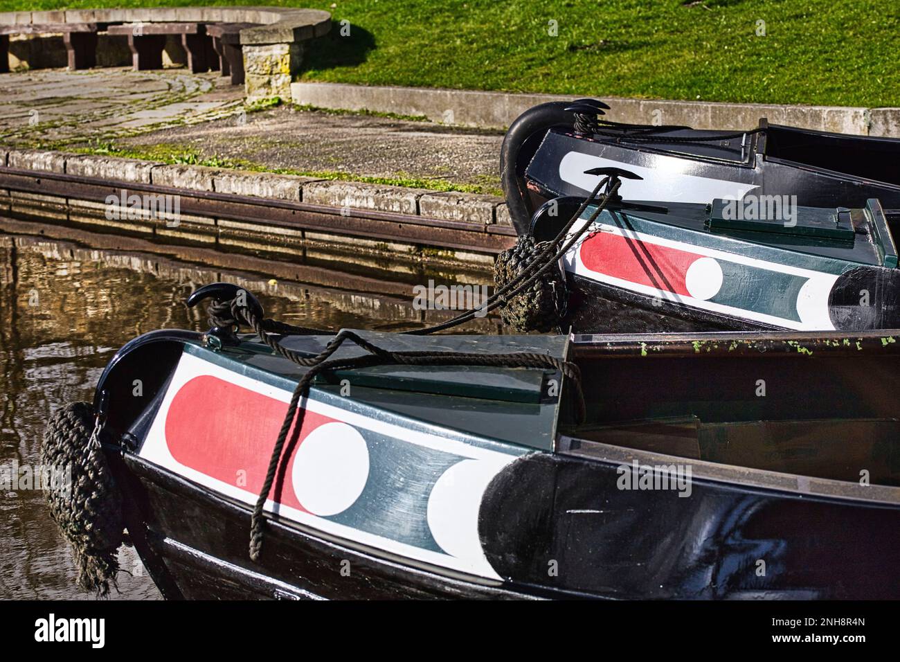 The bows of three narrowboats tethered at a canal side mooring at ...
