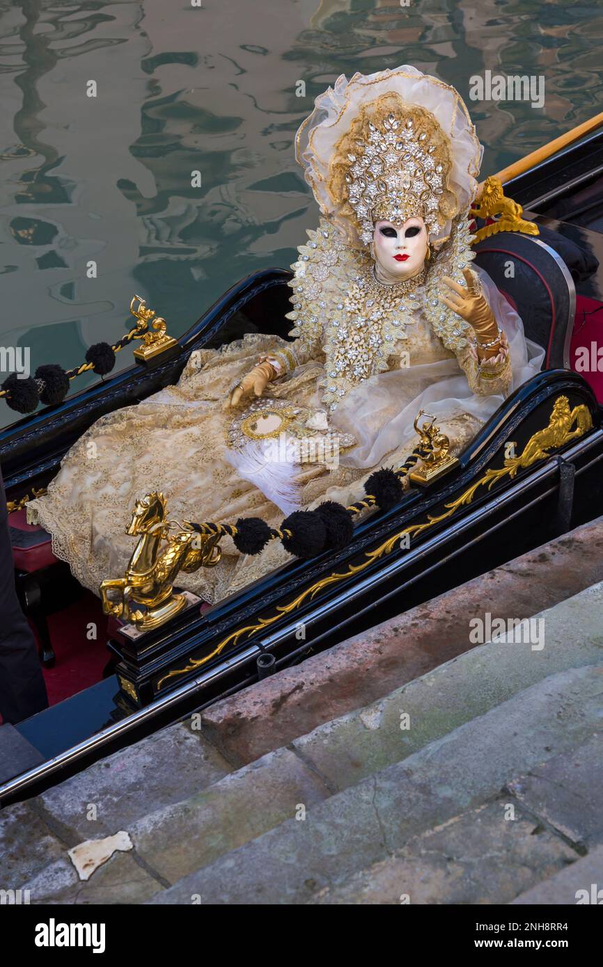 Carnival goer dressed in splendid costume and mask sitting in gondola ...