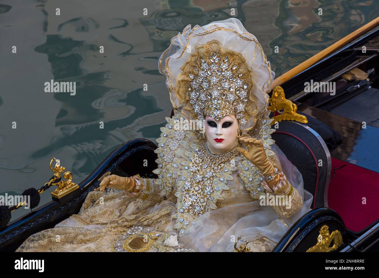 Carnival goer dressed in splendid costume and mask sitting in gondola ...
