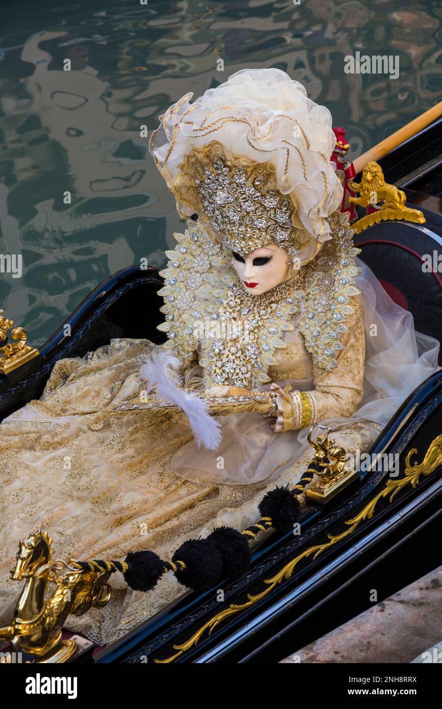 Carnival goer dressed in splendid costume and mask sitting in gondola ...