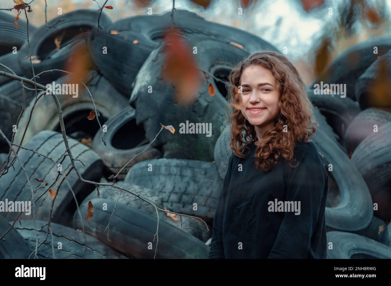 Girl with curly hair and smile on background of pile of rubber tires ...