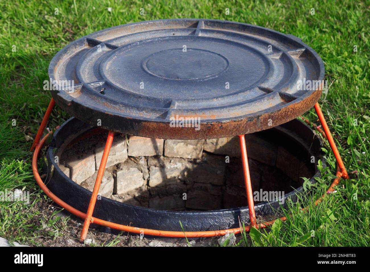 Open well hatch on green lawn. Manhole cover is on stand. Device for ...