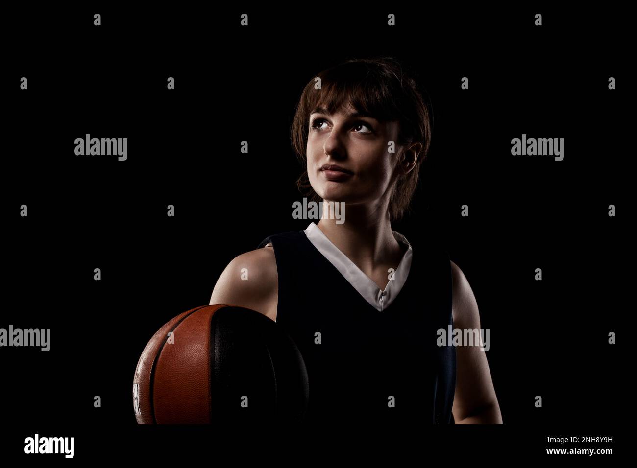 Female basketball player. Beautiful girl holding ball. Side lit half ...