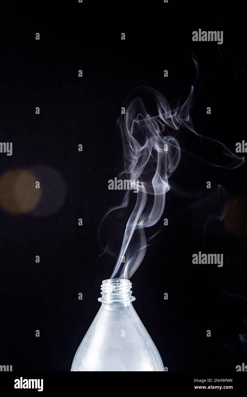 Smoke coming out of a plastic bottle against a black background with ...