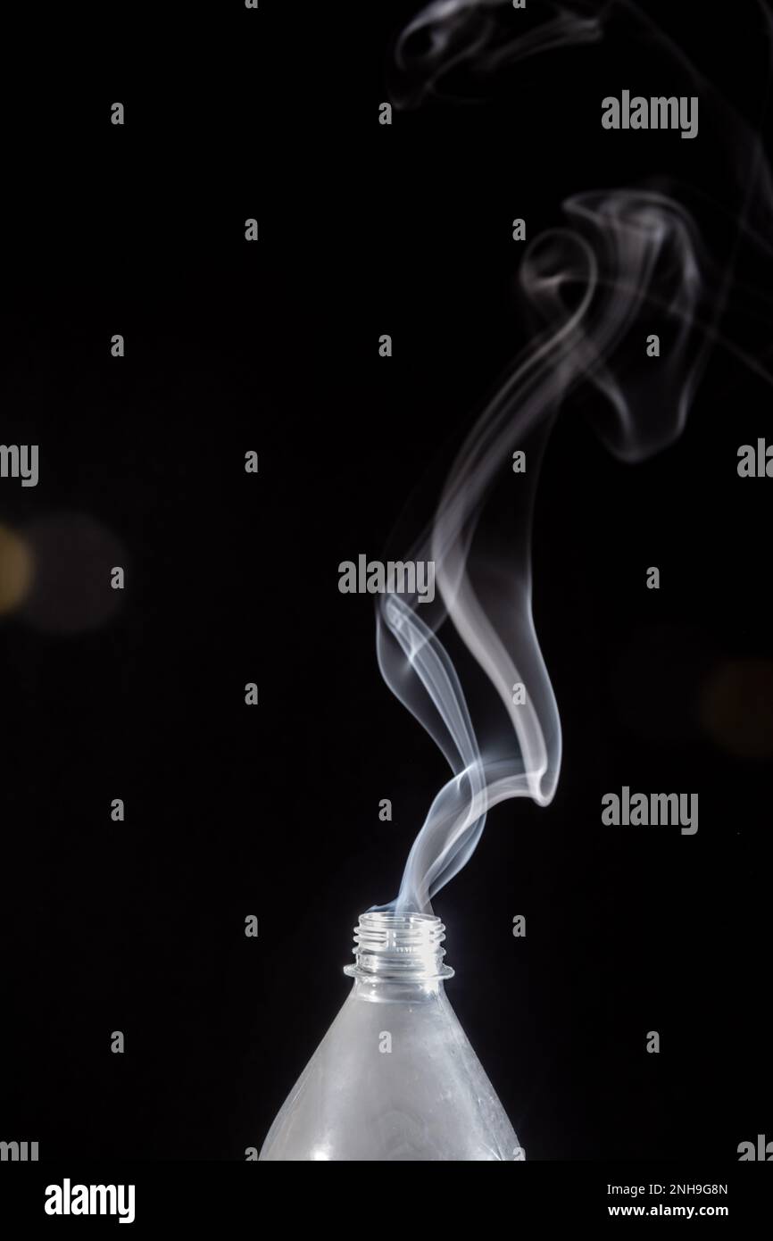 Smoke coming out of a plastic bottle against a black background with ...