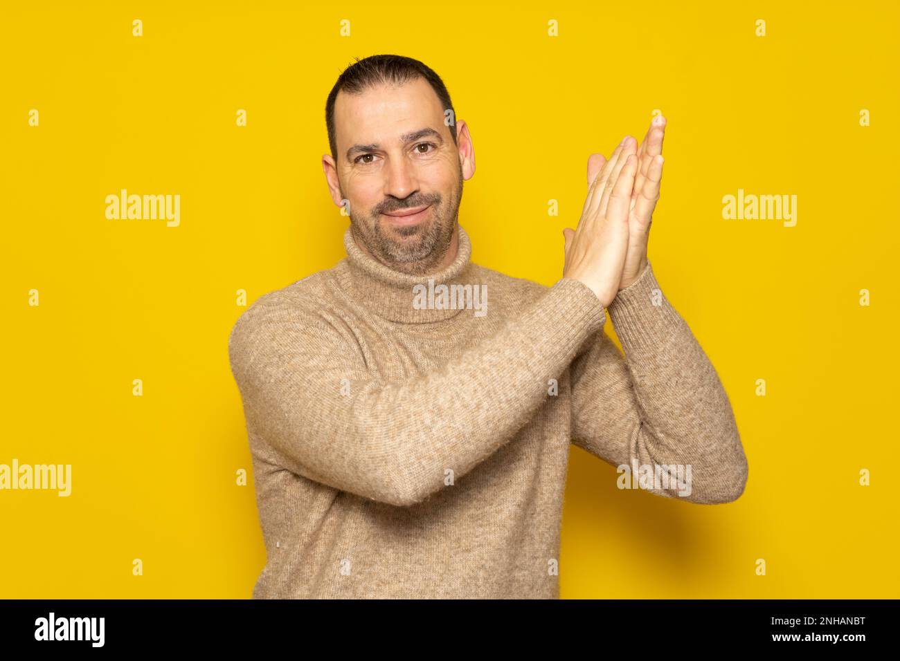 Bearded hispanic man in his 40s wearing a beige turtleneck clapping his ...