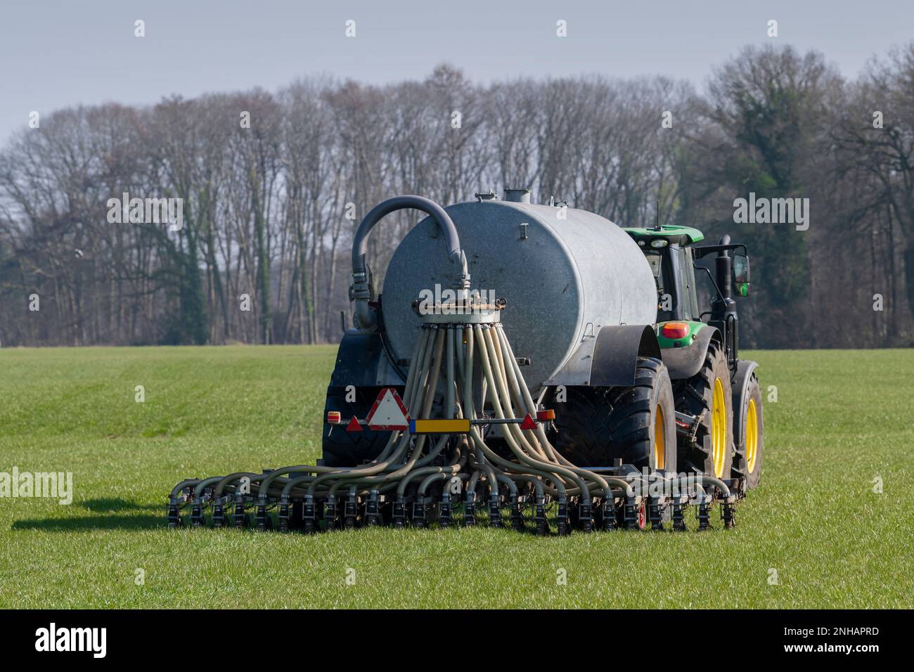 Green tractor with a manure truck on a grass field in the east of the ...