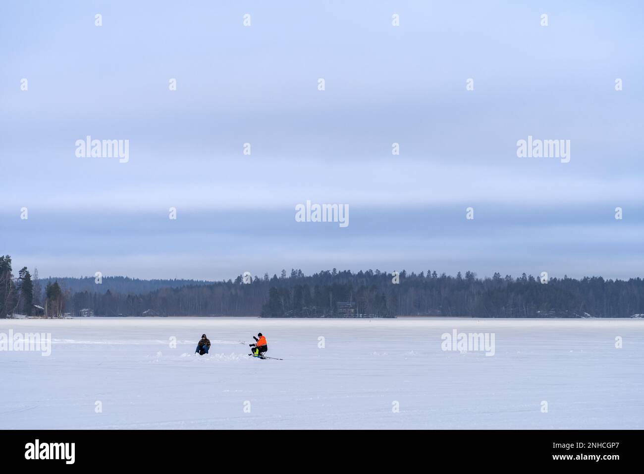 Wintery Finnish lake landscape with two people ice fishing on a frozen ...