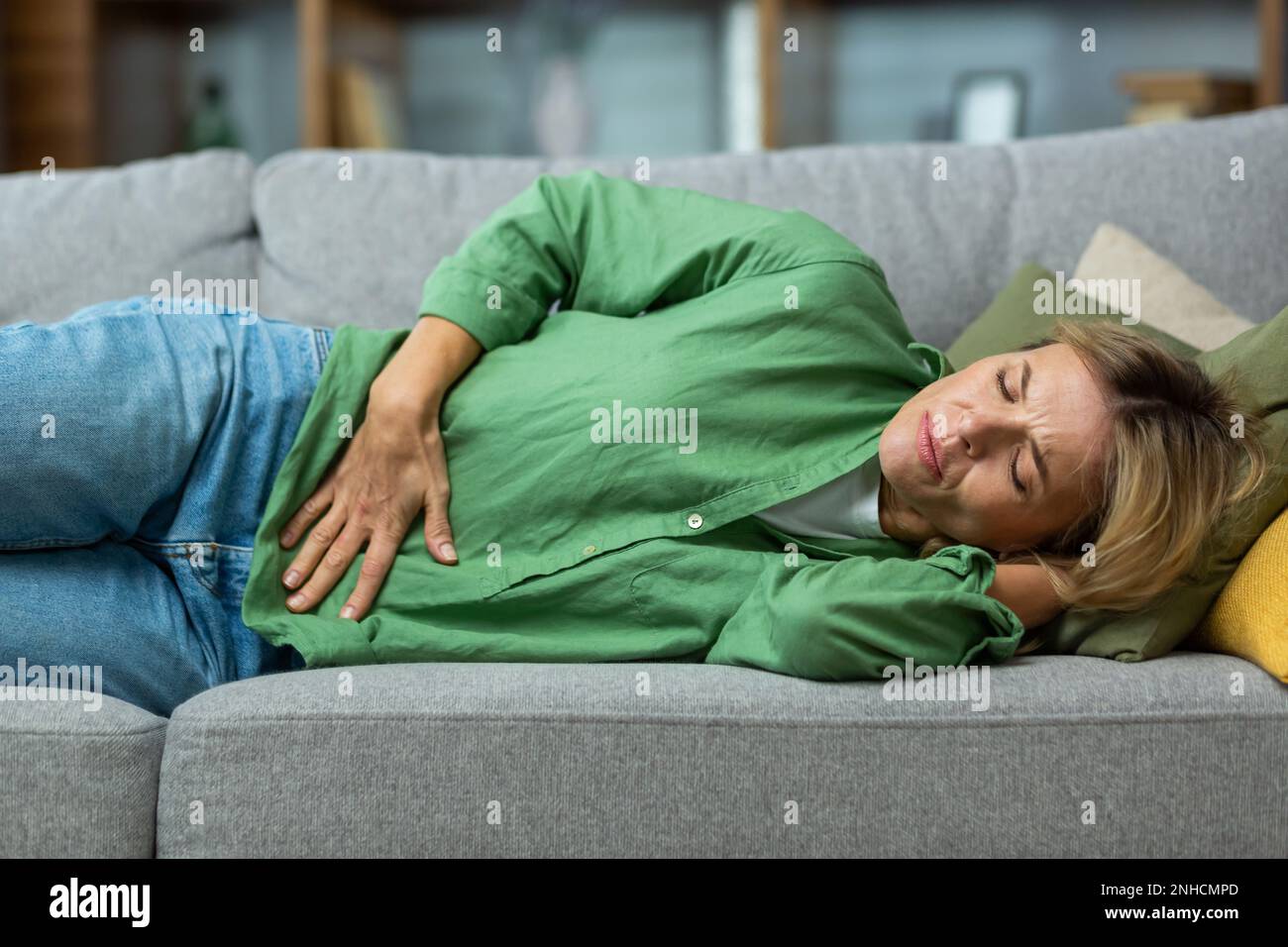 Mature woman alone at home sick, holding hands to side of stomach ...