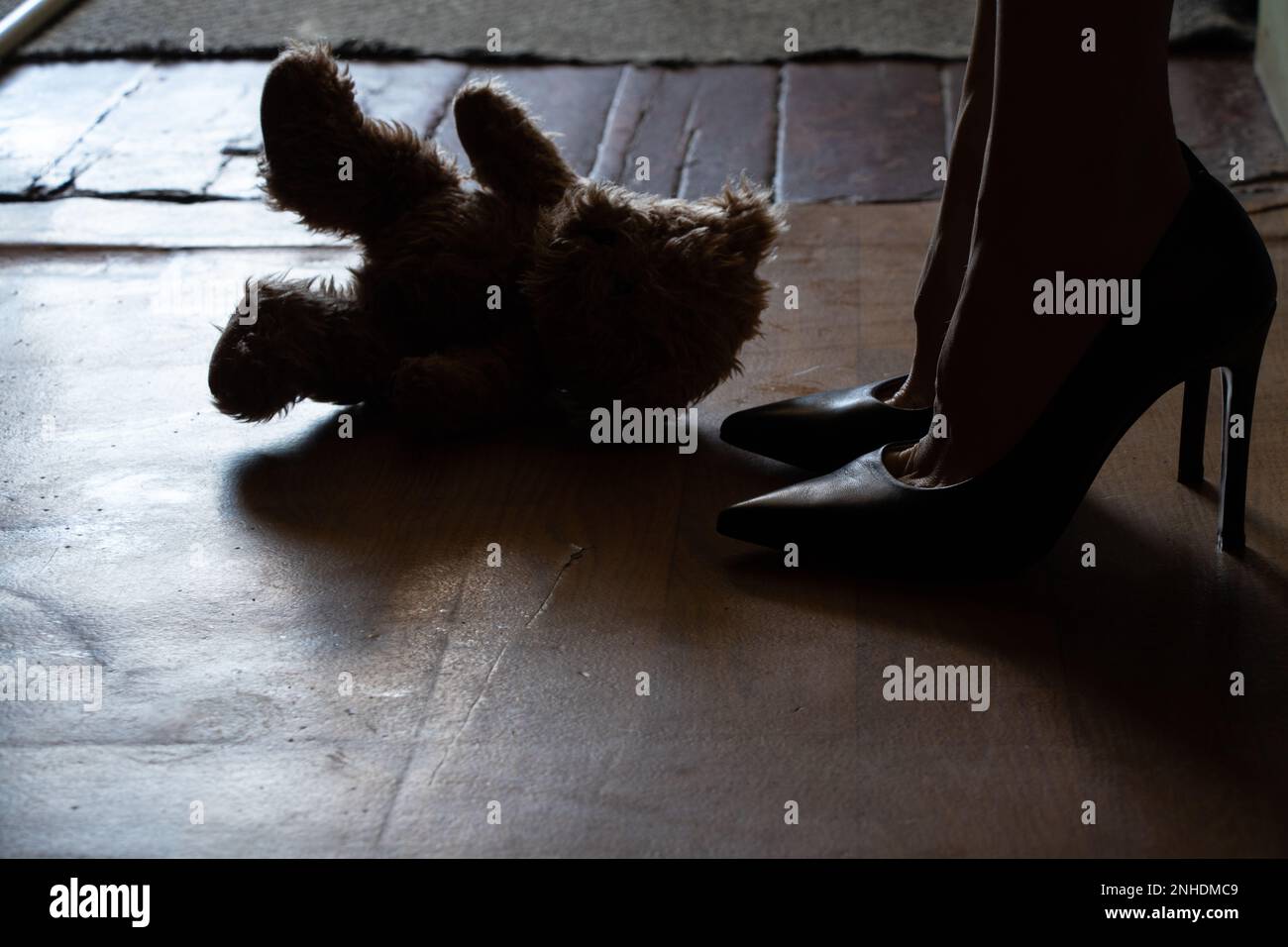female feet next to a baby teddy bear on the floor in the dark in the ...