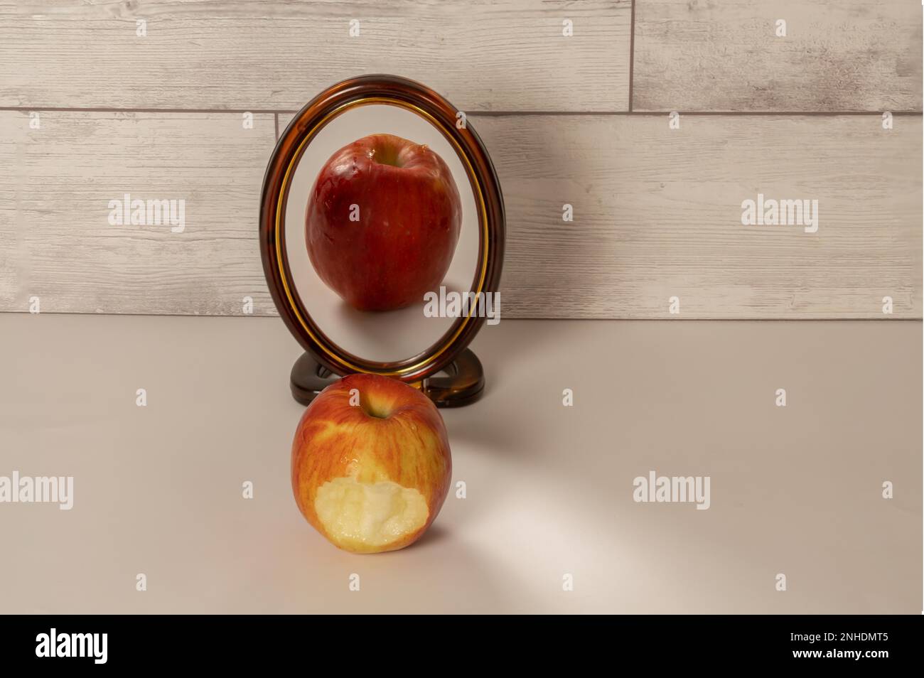 Bitten red apple reflected in a mirror isolated on a white table with ...