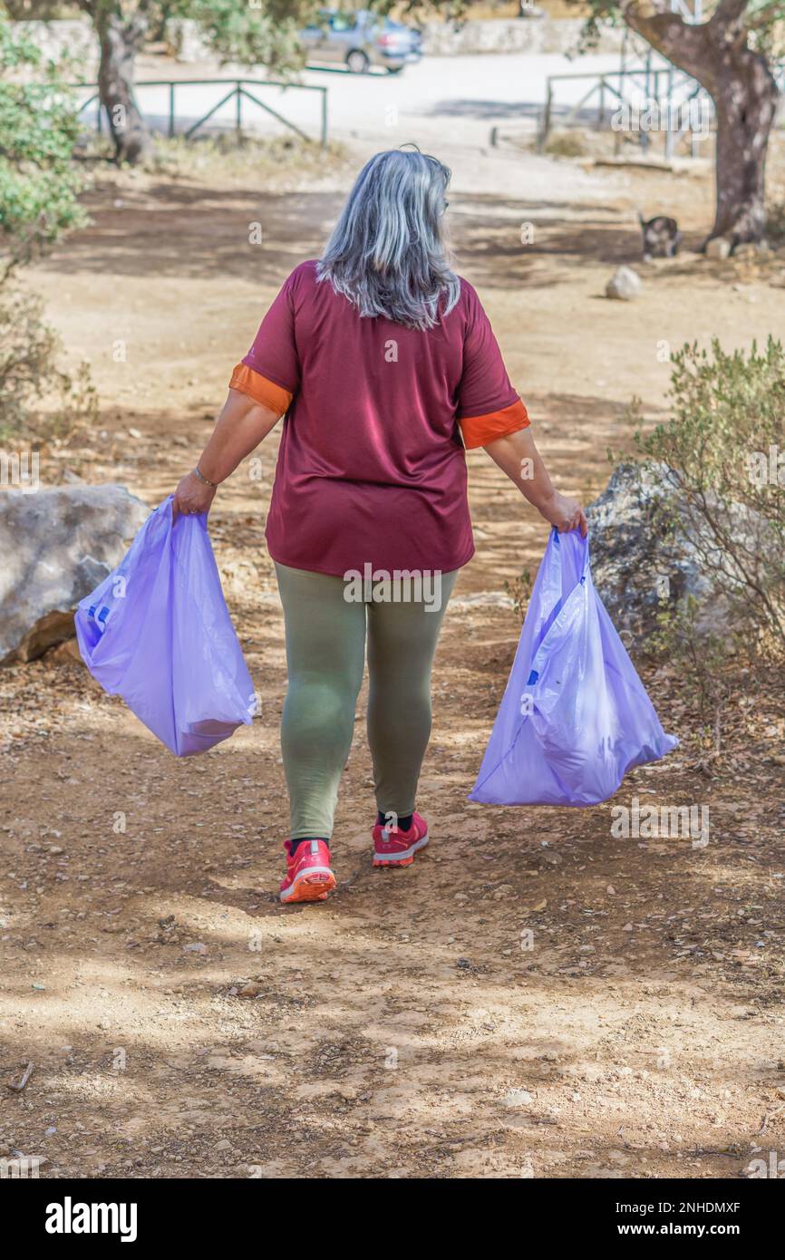 Woman seen from the back carrying bags of garbage collected in the ...